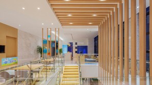 Um hall de hotel moderno com escada de vidro, painéis de madeira e paredes de mármore.