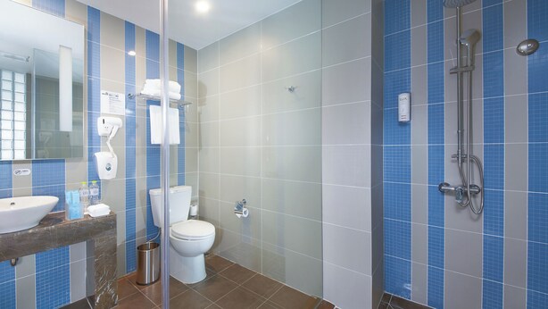 Uma casa de banho moderna com chuveiro em cabine de vidro, sanita branca e bancada de mármore com lavatório.