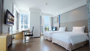Quarto de hotel moderno com escrivaninha, duas camas, televisão e uma janela grande.