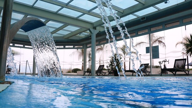 Piscina com jatos de água, espreguiçadeiras e estrutura de teto de vidro.