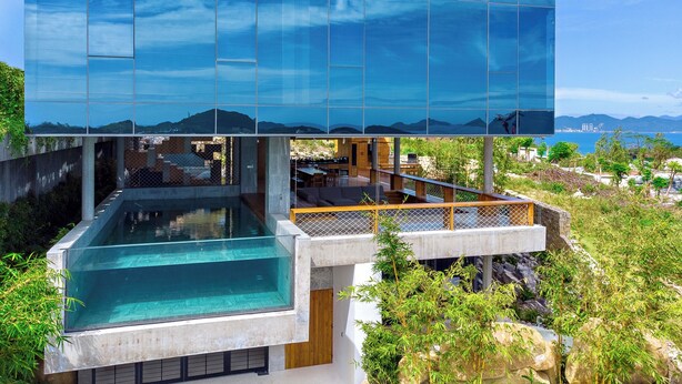 Um edifício moderno com fachada de vidro refletindo o céu e montanhas.