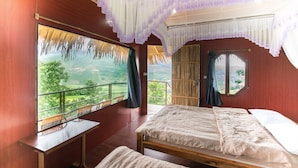 Quarto com cama, mesa e janela com vista para uma paisagem verde.