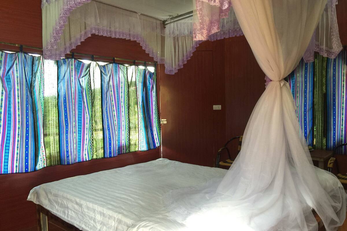 Quarto com cama, janela e cortinas coloridas, além de uma cama com dossel.