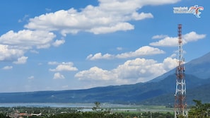 Uma torre de telecomunicações em uma paisagem rural com montanhas e um corpo d'água ao fundo.