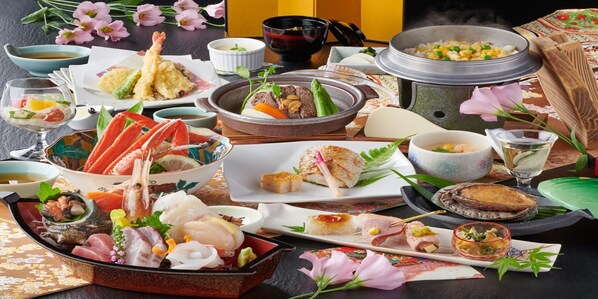 Diversos pratos incluindo frutos do mar, sashimi e tigelas de arroz, dispostos sobre uma mesa com decoração tradicional.