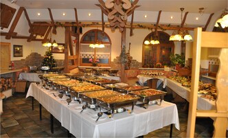 Buffet com várias estações de comida, vigas de madeira e lustres em um interior rústico.