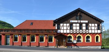 Um edifício tradicional com fachada vermelha e seção superior de estrutura de madeira, com placa indicando uma pousada e um restaurante.