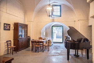 Um quarto espaçoso com um piano de cauda, uma mesa de jantar com cadeiras, um armário e uma grande porta arqueada que dá para área externa.