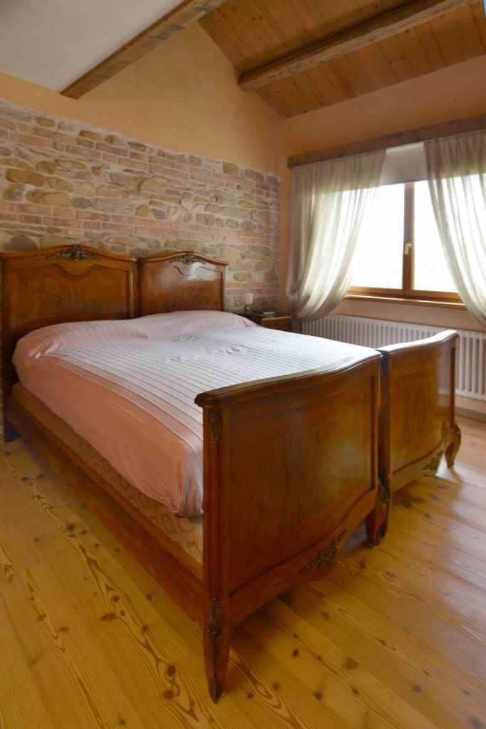 Quarto com cama de madeira, parede de pedra e janela com cortinas.