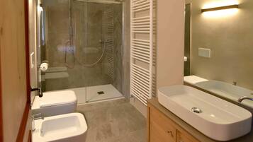 Uma casa de banho com cabine de duche em vidro, pia branca e toucador com espelho.