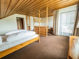 Quarto com cama de madeira, escrivaninha e janela com cortinas.