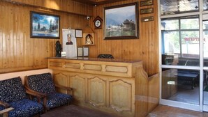 Uma área de recepção com painéis de madeira, um balcão de atendimento, dois sofás estampados e quadros nas paredes.