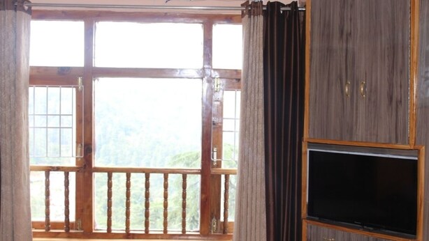 Quarto com uma grande janela, varanda de madeira e televisão de tela plana fixada em um armário de madeira.
