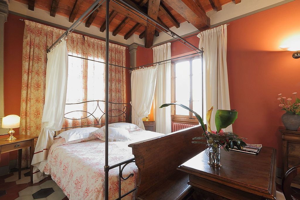 Quarto com cama de dossel, escrivaninha de madeira e um vaso com flores.