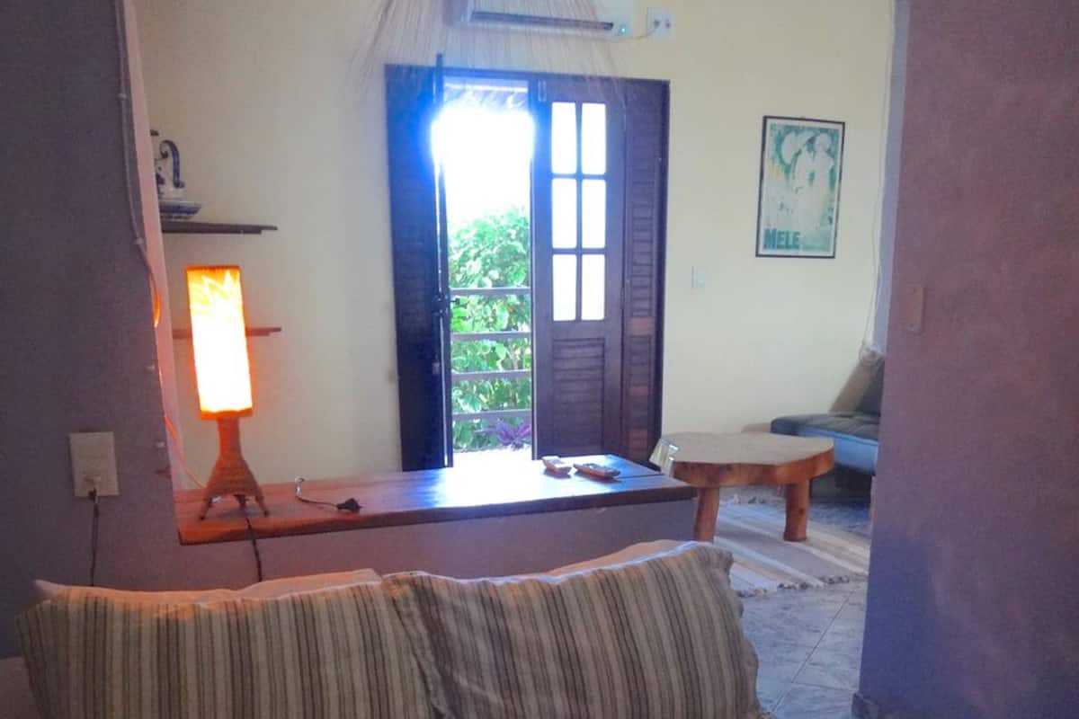 Quarto com sofá listrado, luminária de pé, mesa de madeira e porta que dá para o exterior.