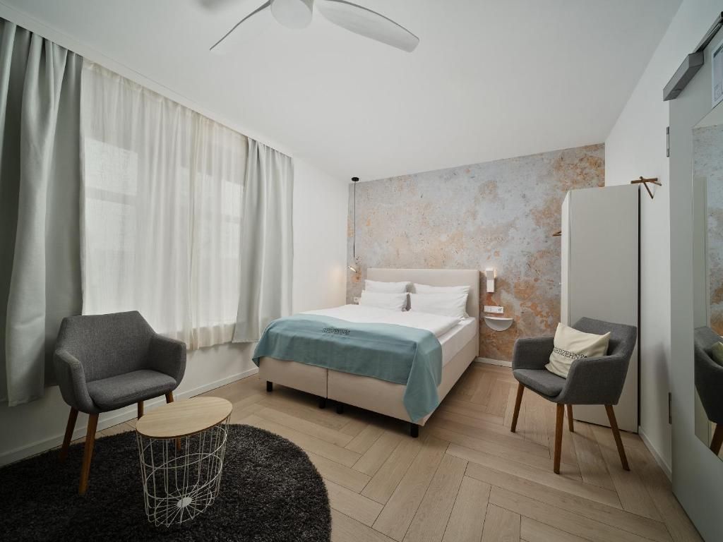 Quarto moderno com cama, duas cadeiras, uma mesinha redonda e um guarda-roupa.