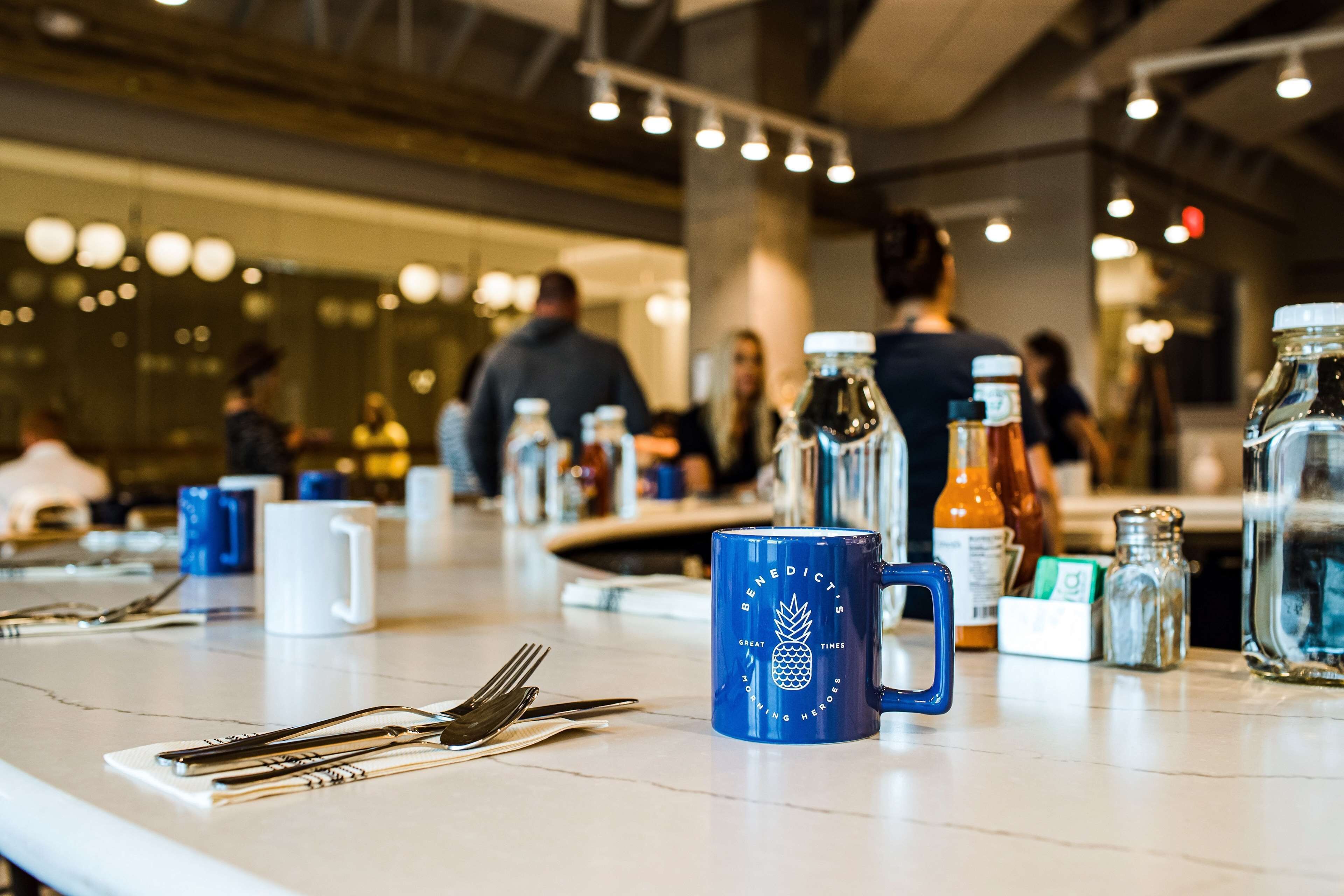 Uma área de bar com um copo azul, utensílios, temperos e uma garrafa de água.