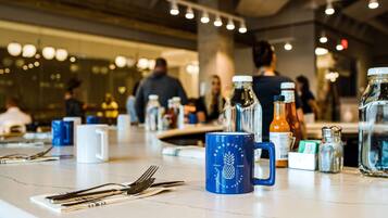 Uma área de bar com um copo azul, utensílios, temperos e uma garrafa de água.