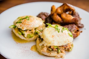 Um prato com dois ovos pochê, vegetais e acompanhamento de batatas assadas.