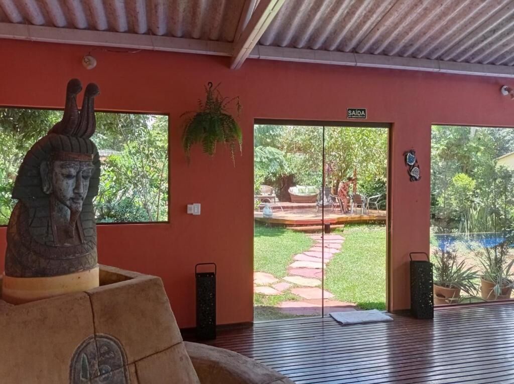 Quarto com uma grande estátua, parede vermelha e porta de vidro que dá para área externa com jardim e caminho.