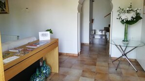 Um corredor com um banco de madeira, uma mesa de vidro com um vaso e um quadro na parede.