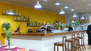 Uma área de bar com balcão central, prateleiras com garrafas e cadeiras de madeira.