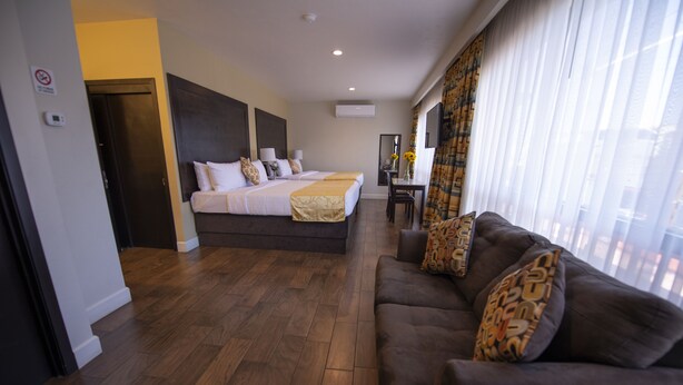 Quarto de hotel com uma cama grande, um sofá, uma escrivaninha com cadeira e uma janela com cortinas.