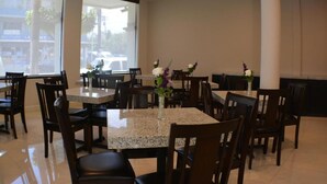 Um restaurante com várias mesas e cadeiras, janelas amplas e um interior limpo e moderno.