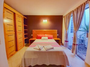 Quarto com cama, guarda-roupa de madeira, mesas de cabeceira e janela com cortinas.