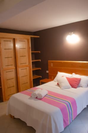 Quarto com cama, guarda-roupa de madeira e mesa de cabeceira.