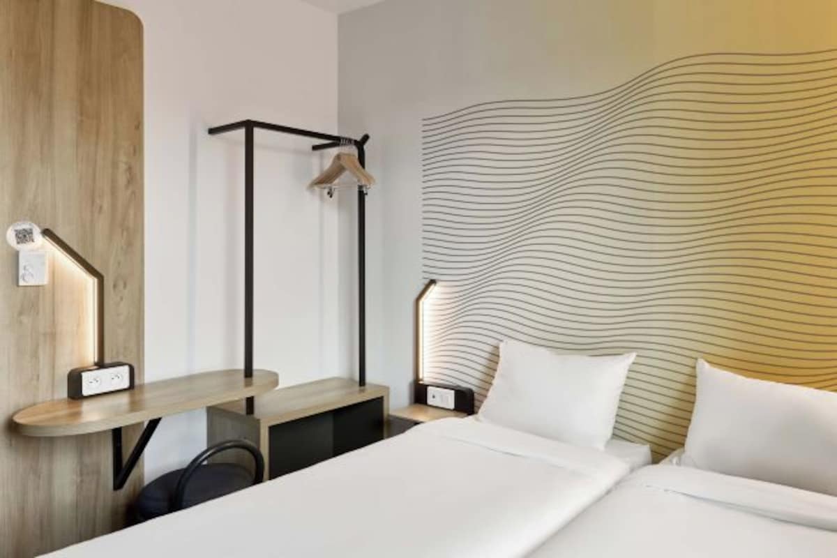 Quarto de hotel com cama, mesas de cabeceira, parede de madeira, cabideiro e um padrão no papel de parede.