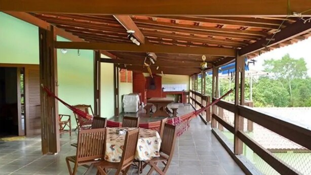 Estarão ao ar livre com cobertura, móveis de madeira e uma rede.