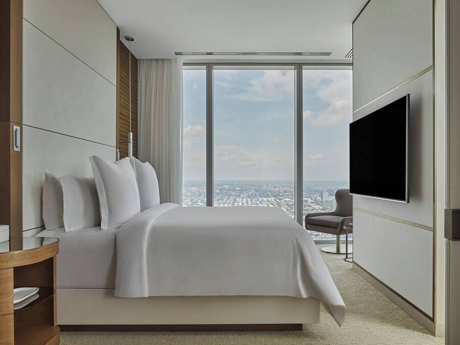 Quarto de hotel moderno com uma cama grande, televisão e vista para a cidade.