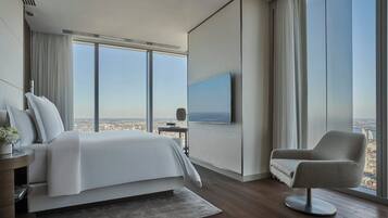 Quarto de hotel moderno com uma cama grande, televisão, cadeira e vista da cidade.