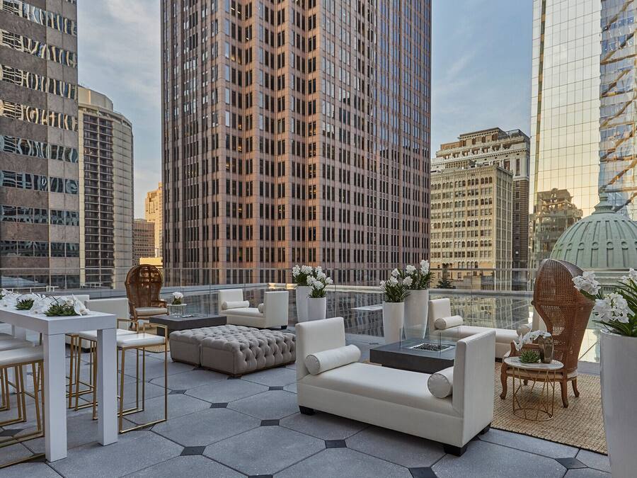 Um lounge no terraço com móveis modernos, grandes vasos de plantas e vista para a cidade.