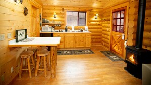 Interior de uma cabana de tronco com cozinha, incluindo fogão, micro-ondas e banquinhos de madeira.