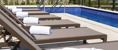 Uma área na beira da piscina com espreguiçadeiras, toalhas e vista para a piscina.