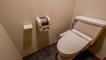 Casa de banho pequena e compacta com sanita, dispensador de papel e botão de descarga na parede.