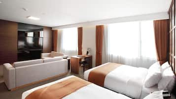 Quarto de hotel com duas camas, um sofá, uma escrivaninha e uma televisão.