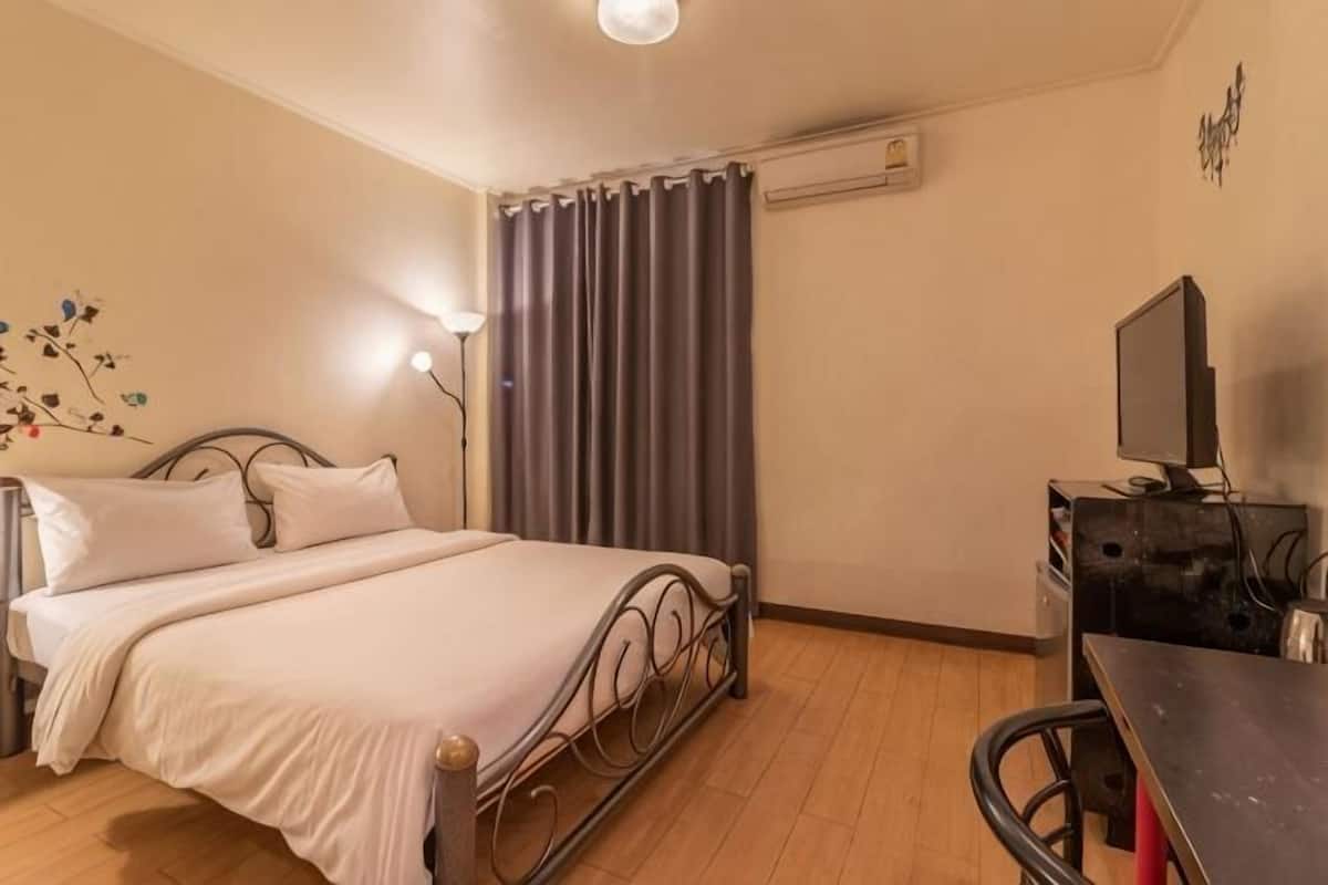 Quarto com cama, escrivaninha, cadeira, abajur e televisão.