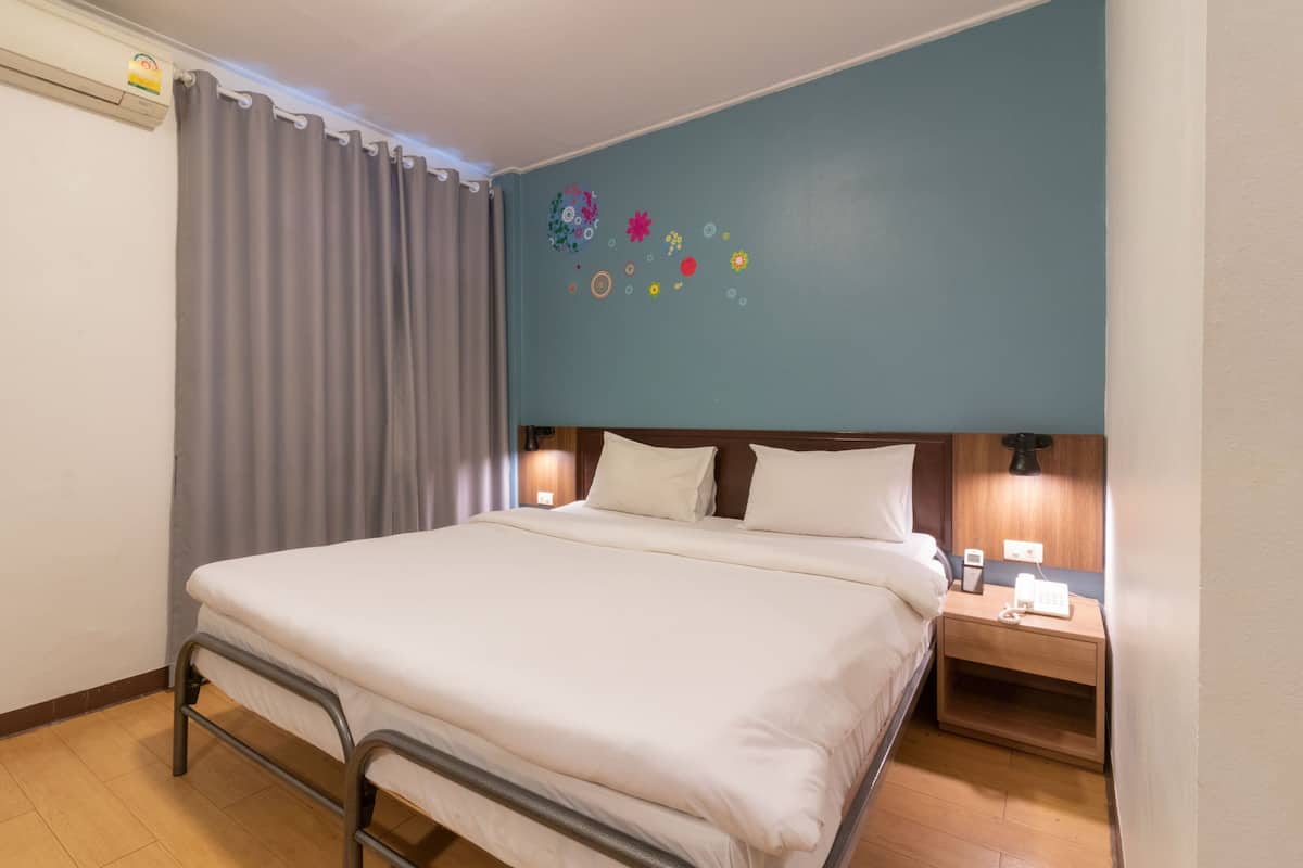 Quarto de hotel com cama, mesa de cabeceira, abajur e um objeto decorativo na parede.