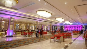 Um amplo saguão de hotel com área de bar central, diversos espaços de estar e um lustre decorativo.