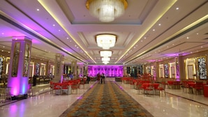 Um amplo hall de hotel com palco central, cadeiras vermelhas e carpete estampado.