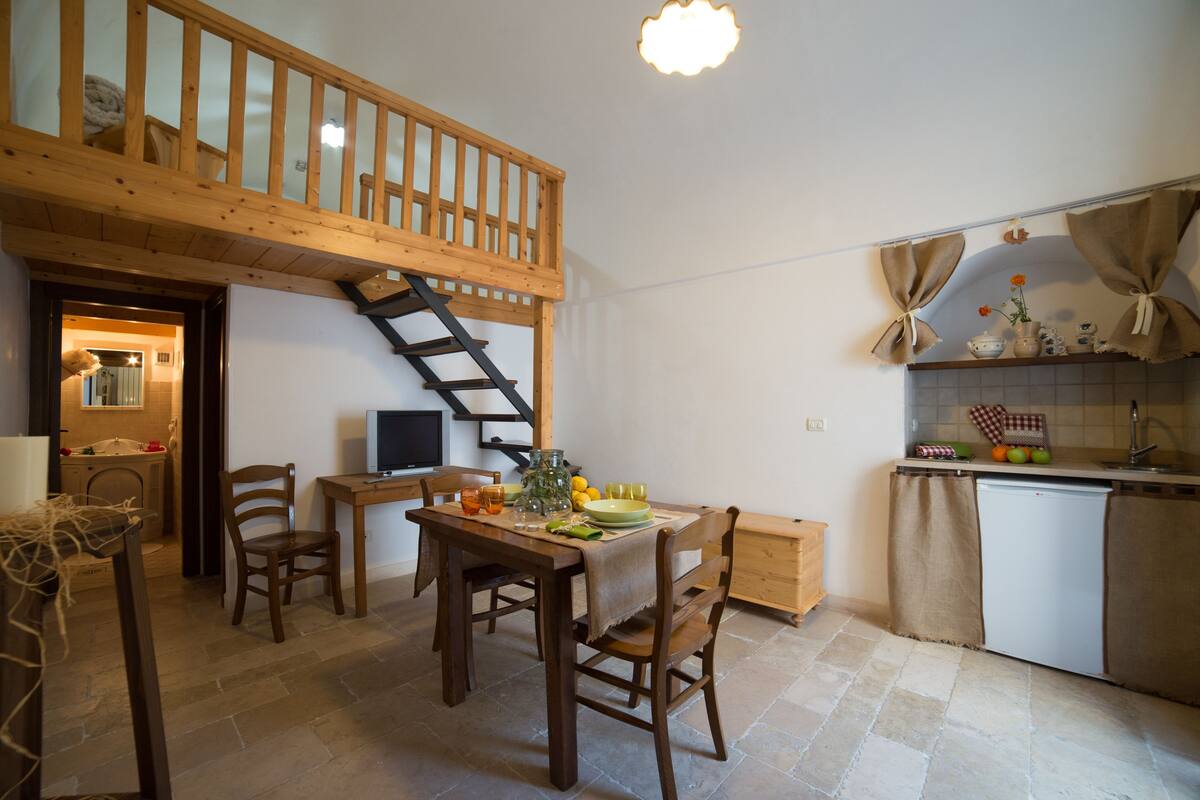 Uma cozinha com mesa de jantar, cadeiras, escada e um pequeno espaço com pia e bancada.