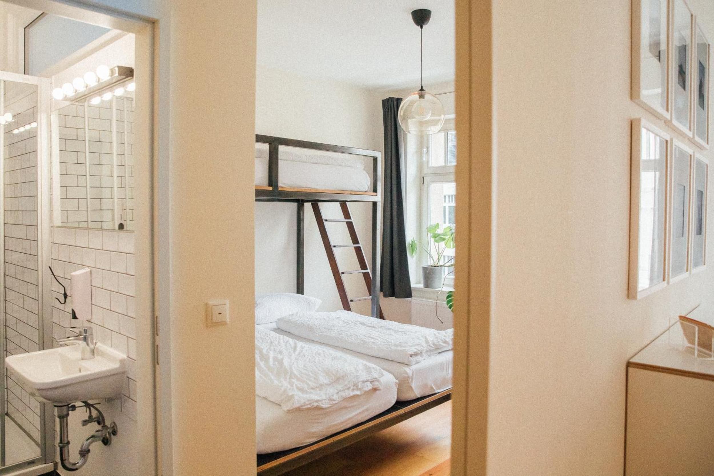Corredor estreito que dá para um quarto com beliche, janela com cortinas e luminária pendente.