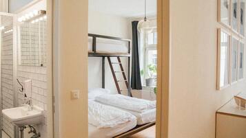 Corredor estreito que dá para um quarto com beliche, janela com cortinas e luminária pendente.