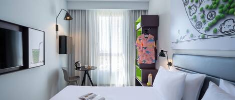 Quarto de hotel com cama, televisão, escrivaninha e janela com cortinas.