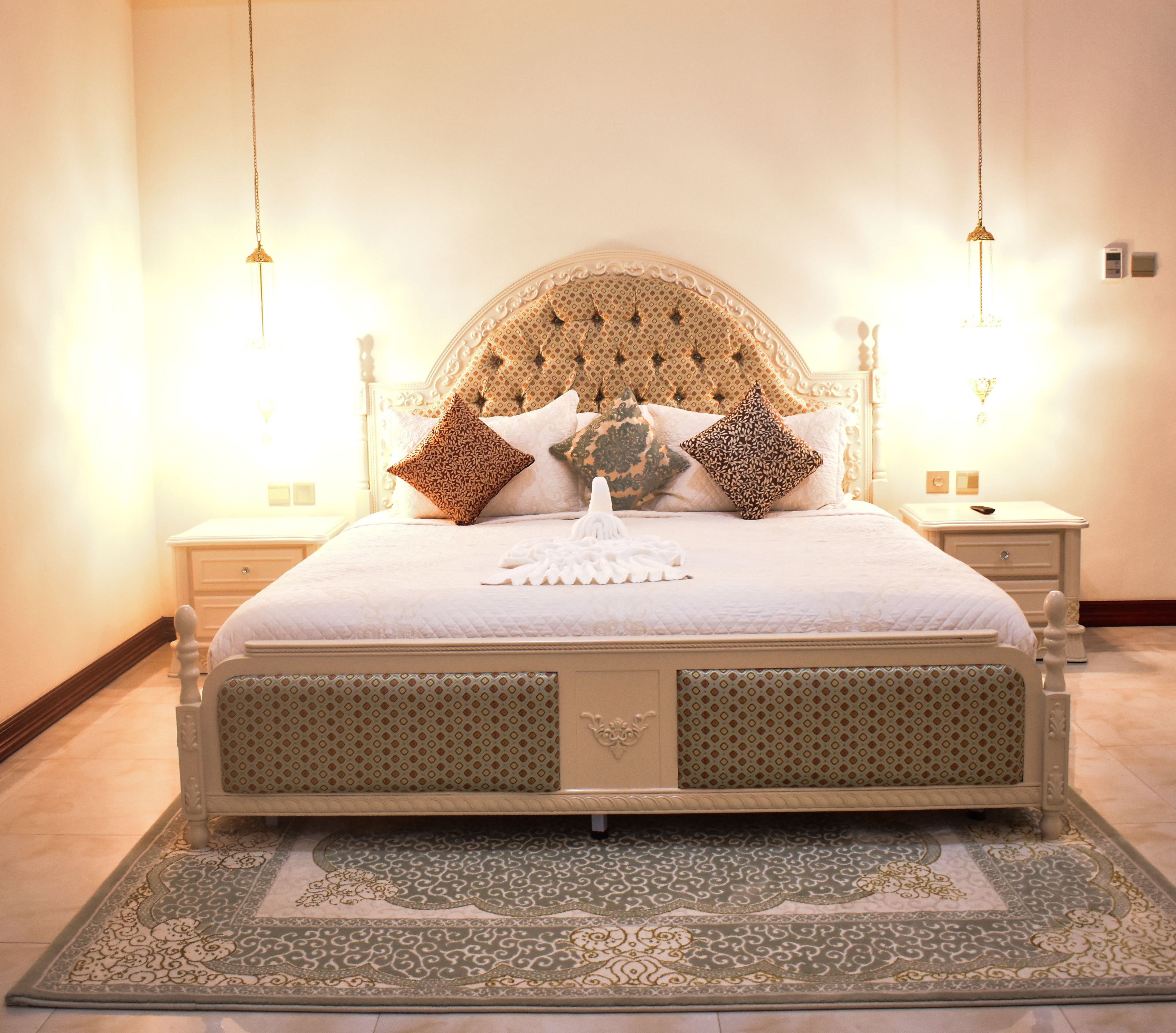Uma cama grande com cabeceira estofada, duas mesas de cabeceira e um tapete decorativo.