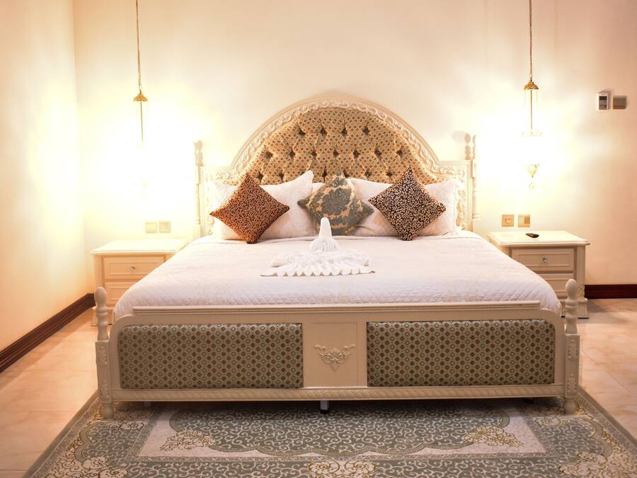 Uma cama grande com cabeceira estofada, duas mesas de cabeceira e um tapete decorativo.