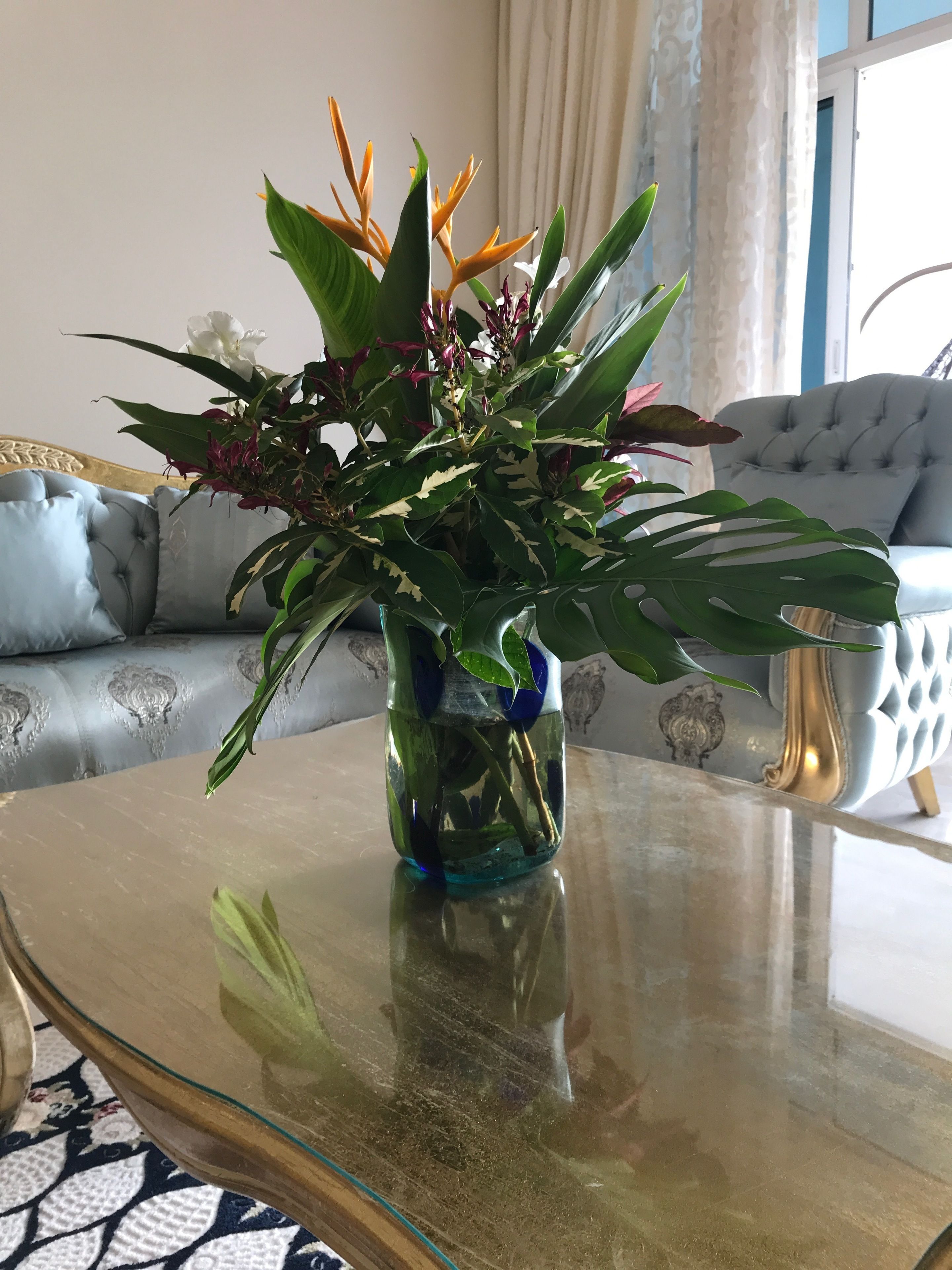 Uma mesa de vidro com um vaso de plantas em um quarto com sofá e cortinas.